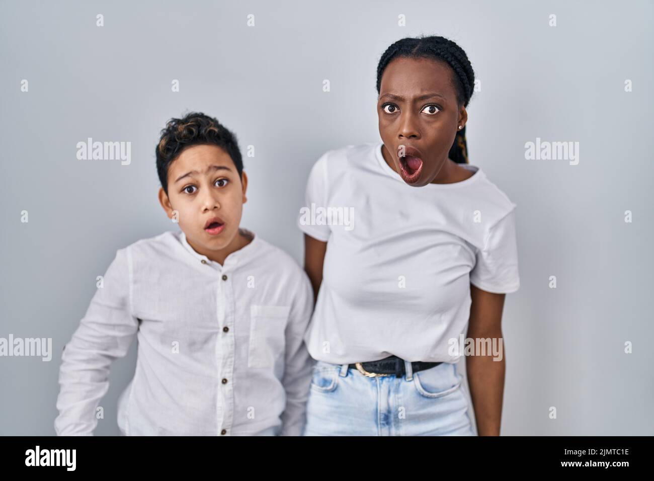 Young mother and son standing together over white background in shock ...