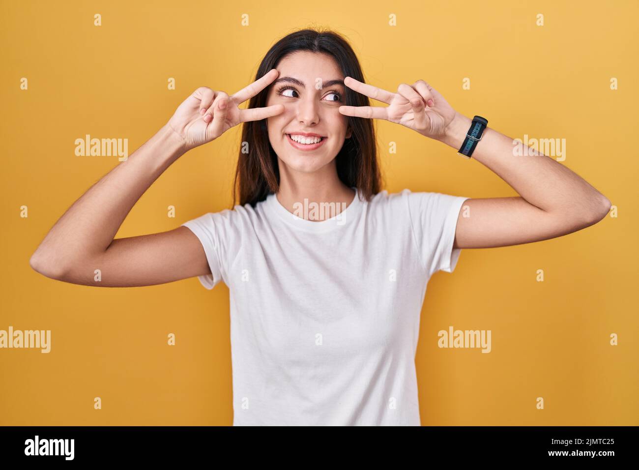 Young beautiful woman standing over yellow background doing peace ...