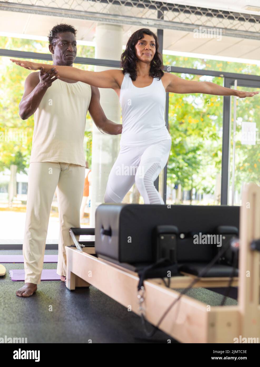 Woman coach helping man and woman in pilates workout Stock Photo - Alamy