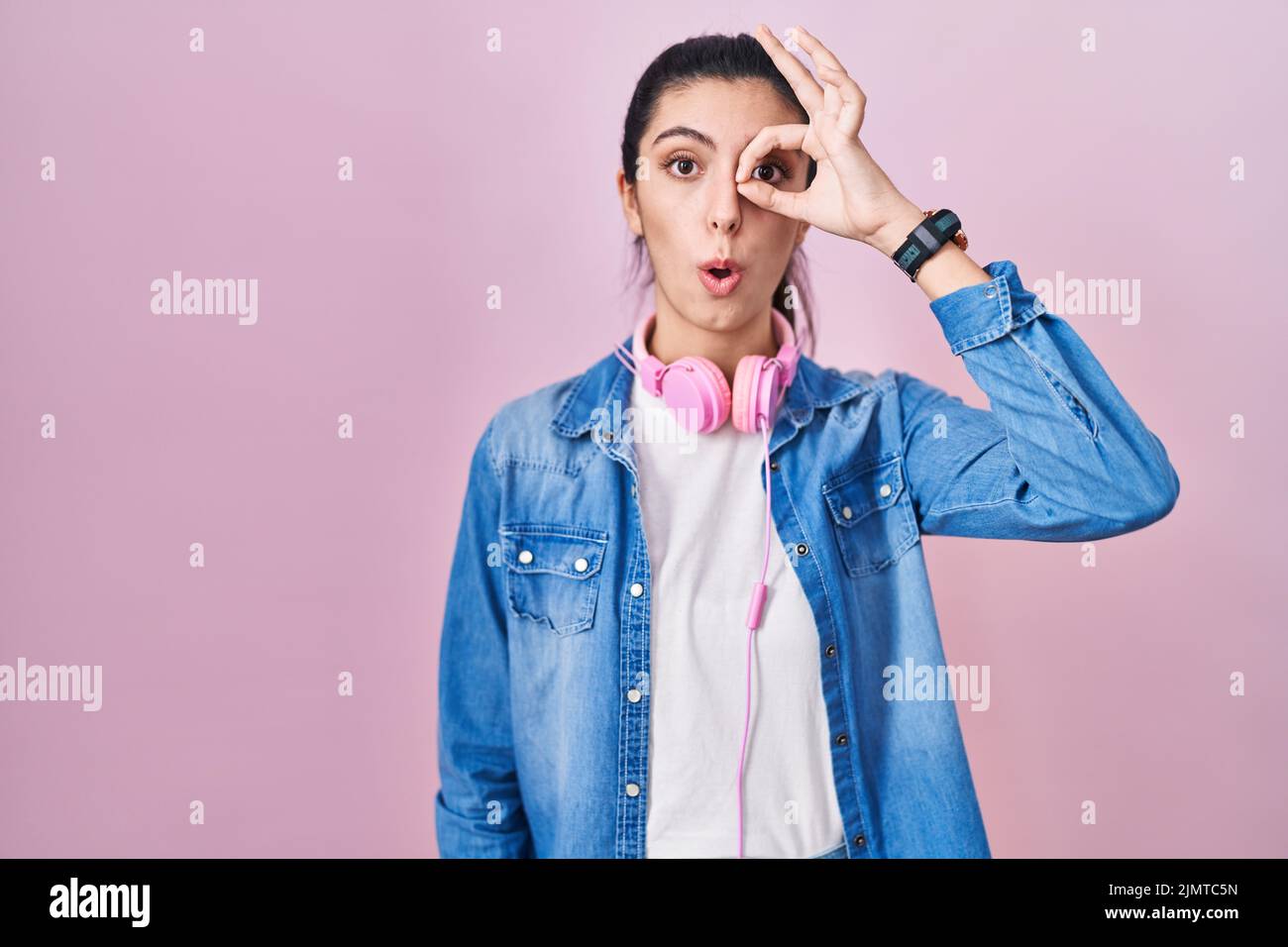 Young beautiful woman standing over pink background doing ok gesture ...