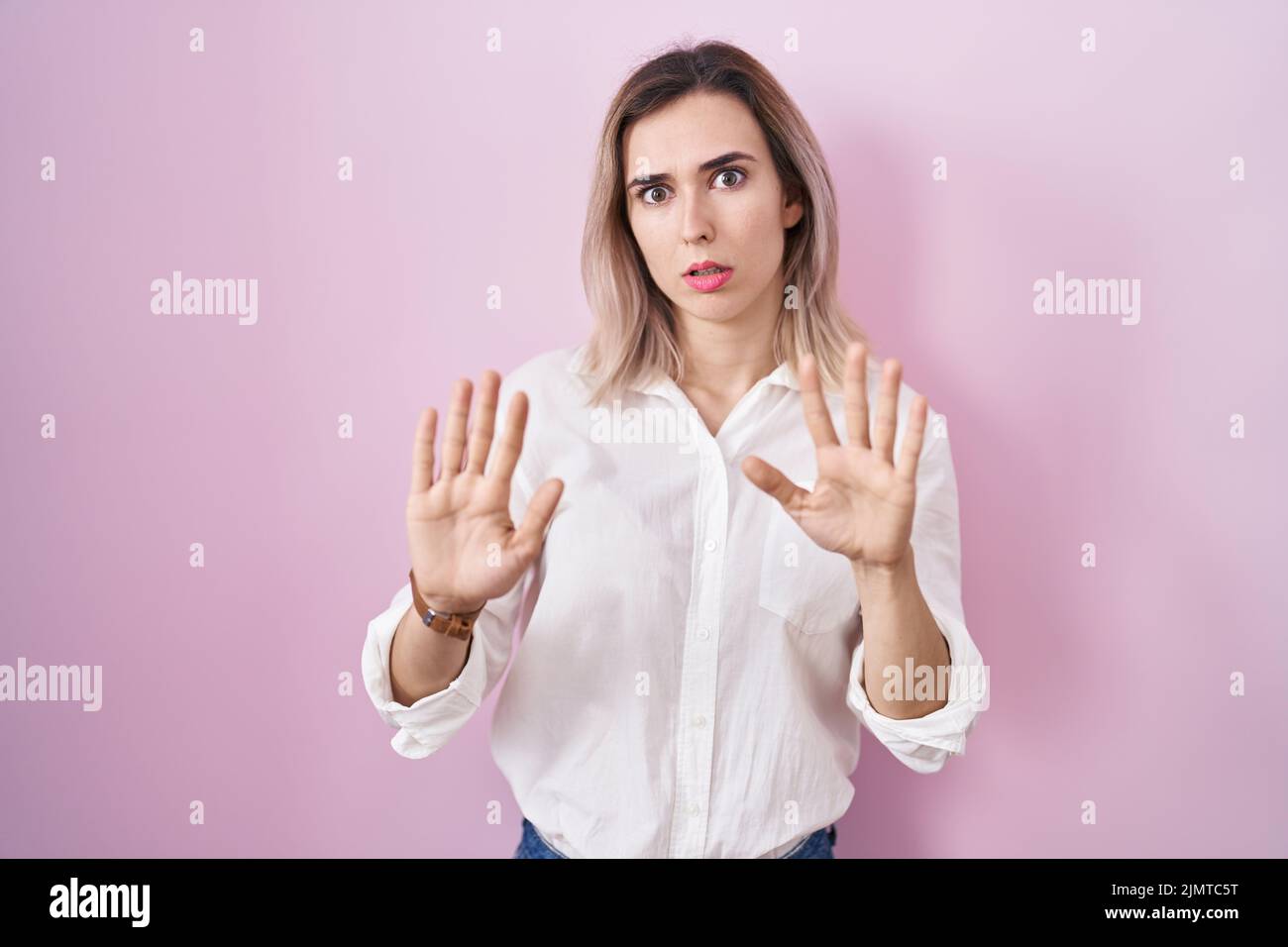 Young beautiful woman standing over pink background moving away hands ...