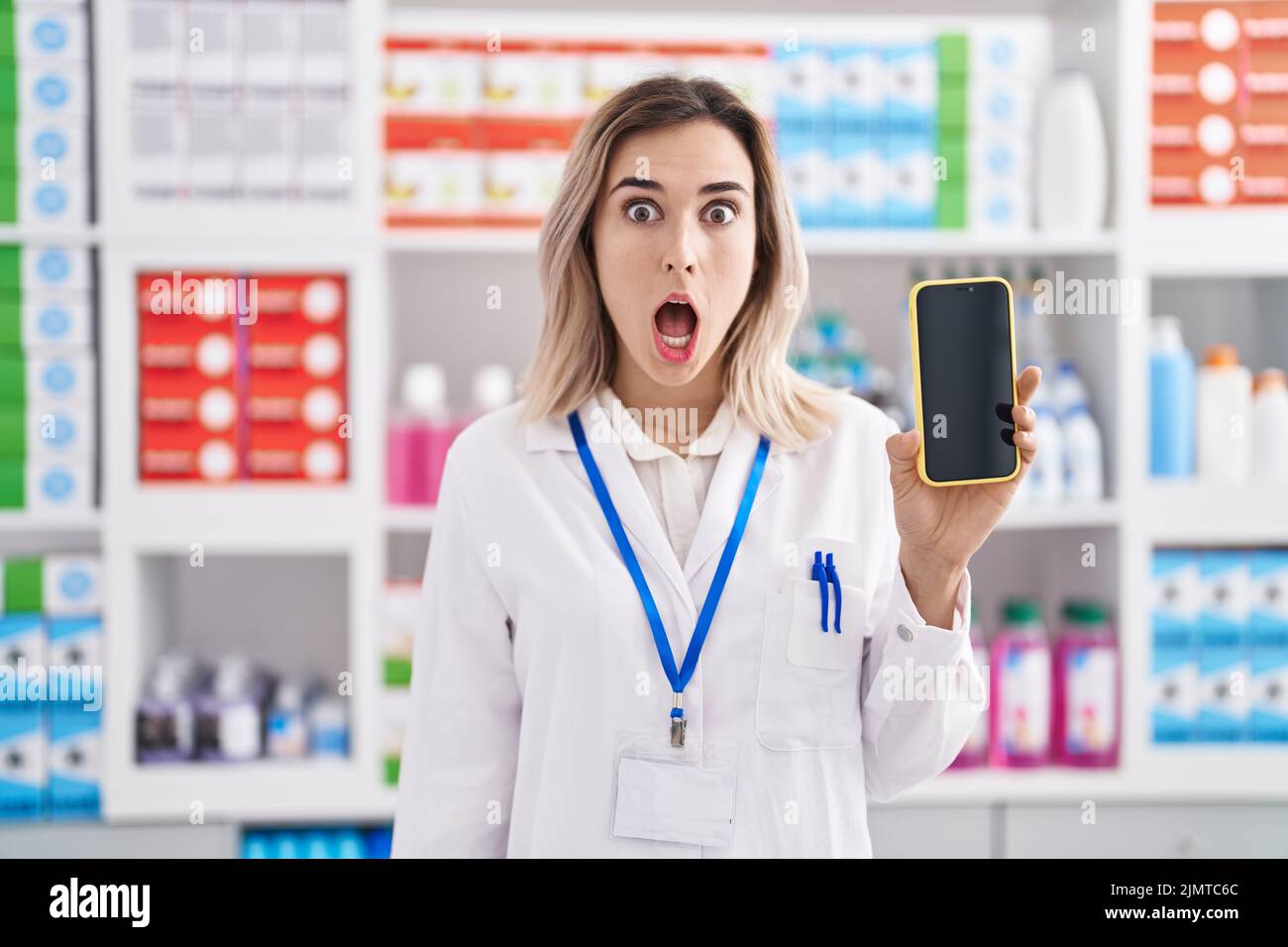 Young beautiful woman working at pharmacy drugstore showing smartphone ...