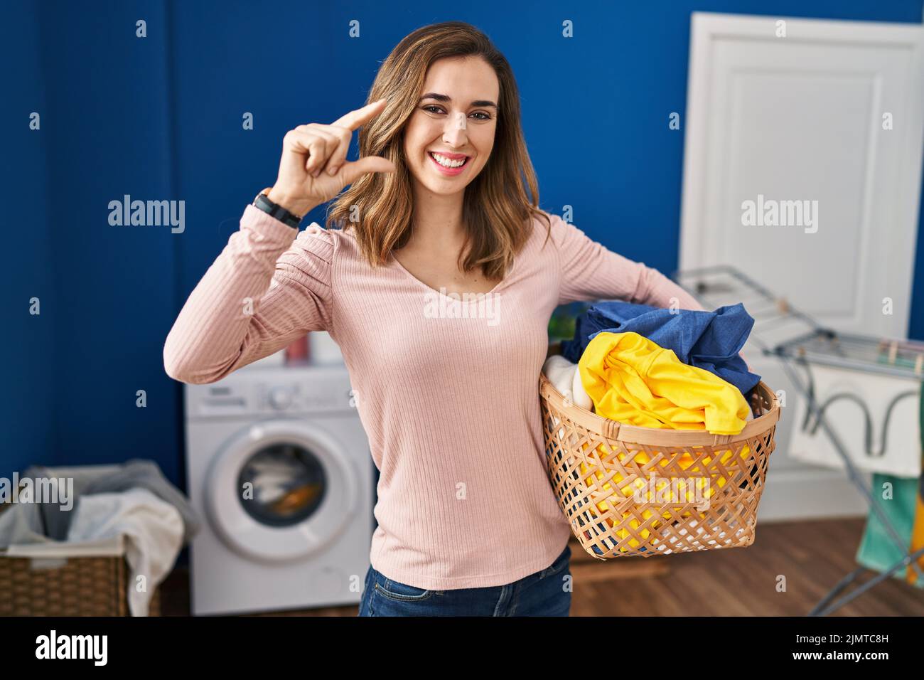 Young woman holding laundry basket smiling and confident gesturing with ...