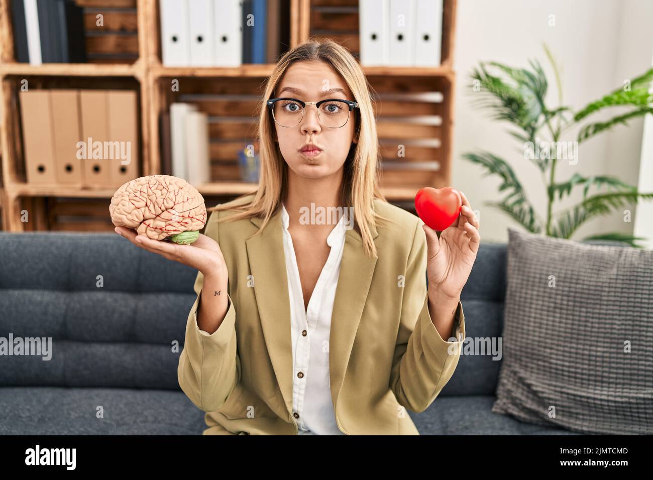 Young blonde woman working at therapy office holding brain and health ...