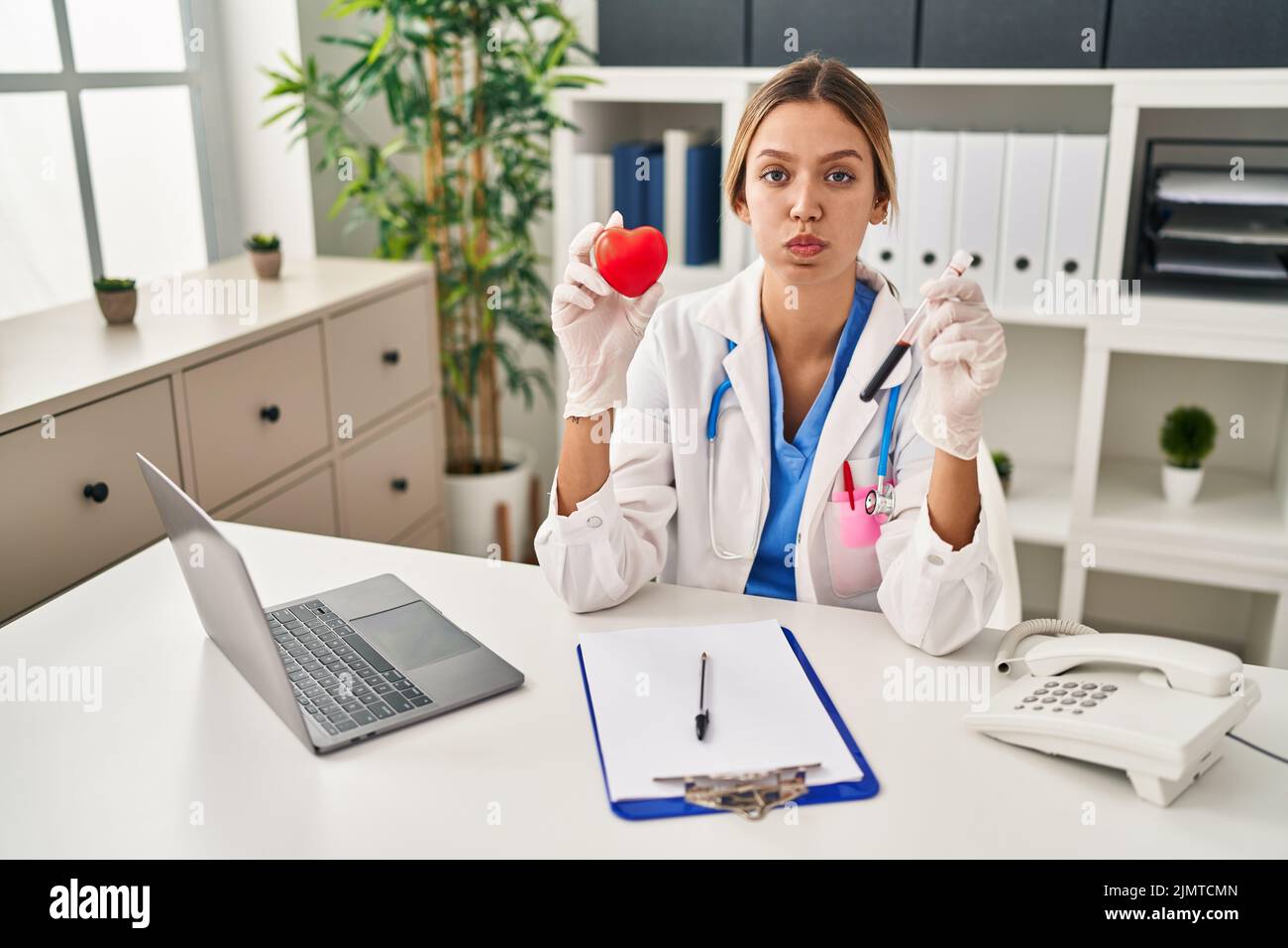 Young blonde woman wearing doctor uniform holding blood and heart ...