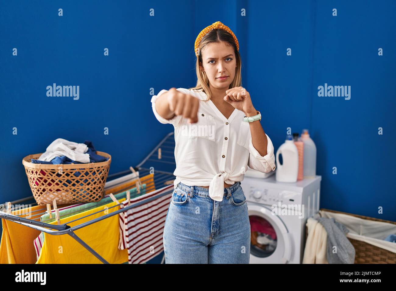 Young blonde woman at laundry room punching fist to fight, aggressive ...