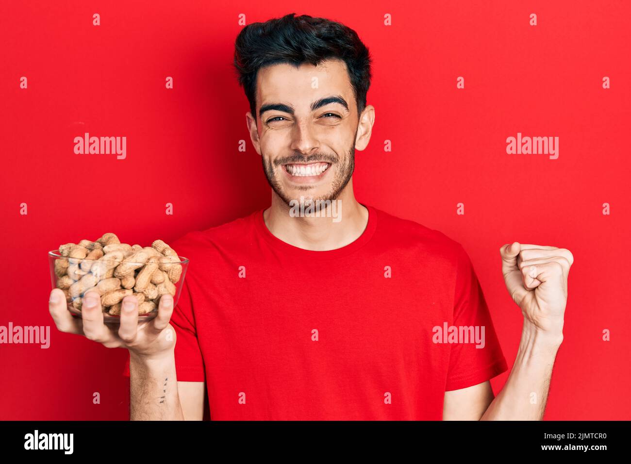 Young hispanic man holding peanuts screaming proud, celebrating victory ...