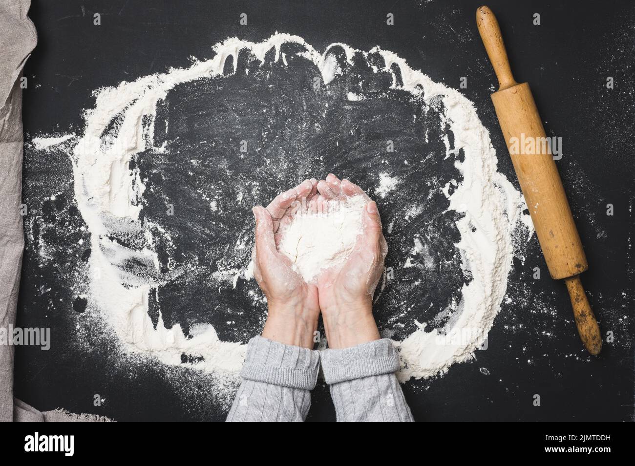 Two female hands hold a handful of white wheat flour on a black table ...