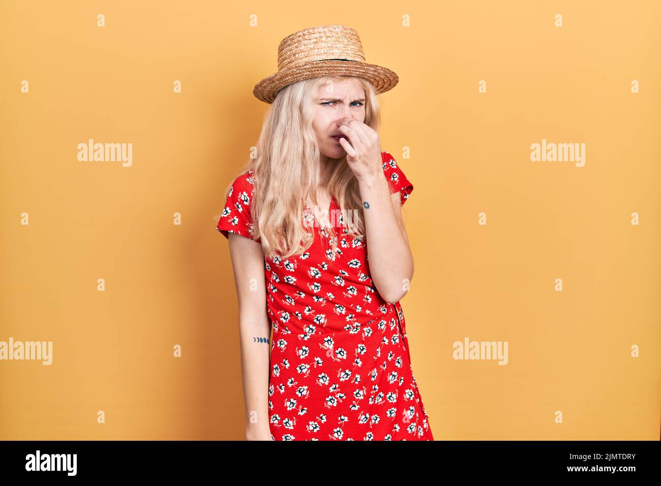 Beautiful caucasian woman with blond hair wearing summer hat smelling ...