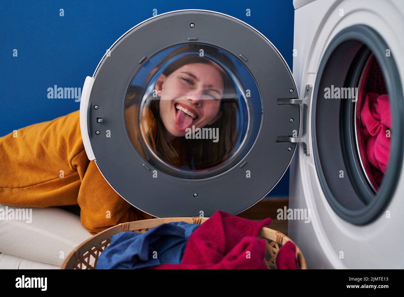 Young brunette woman looking through the washing machine window ...