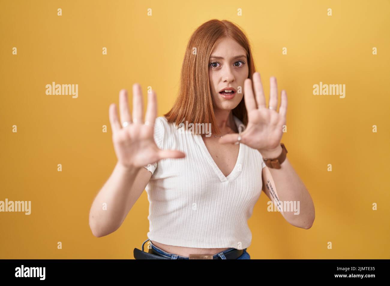 Young redhead woman standing over yellow background afraid and ...