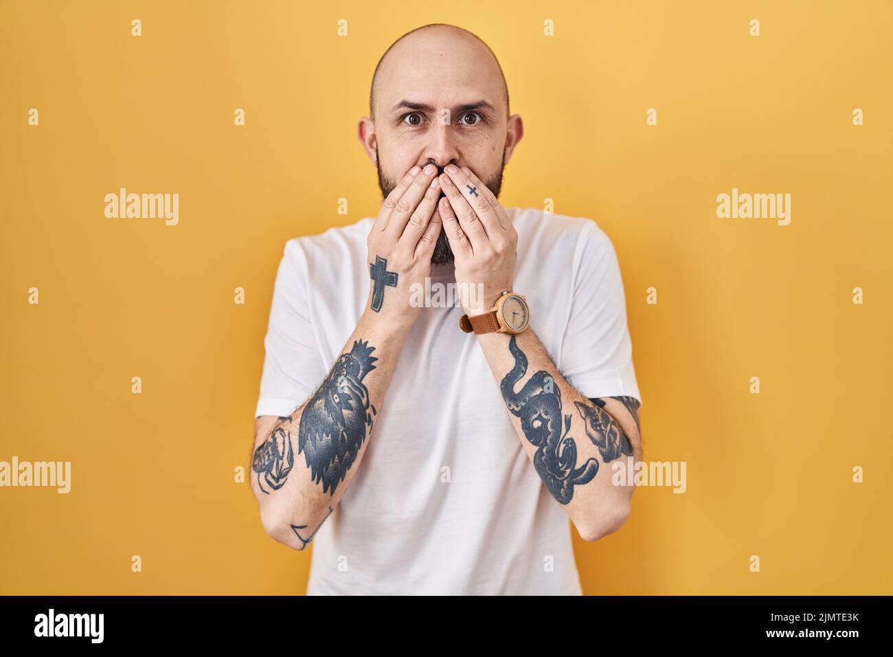 Young hispanic man with tattoos standing over yellow background ...