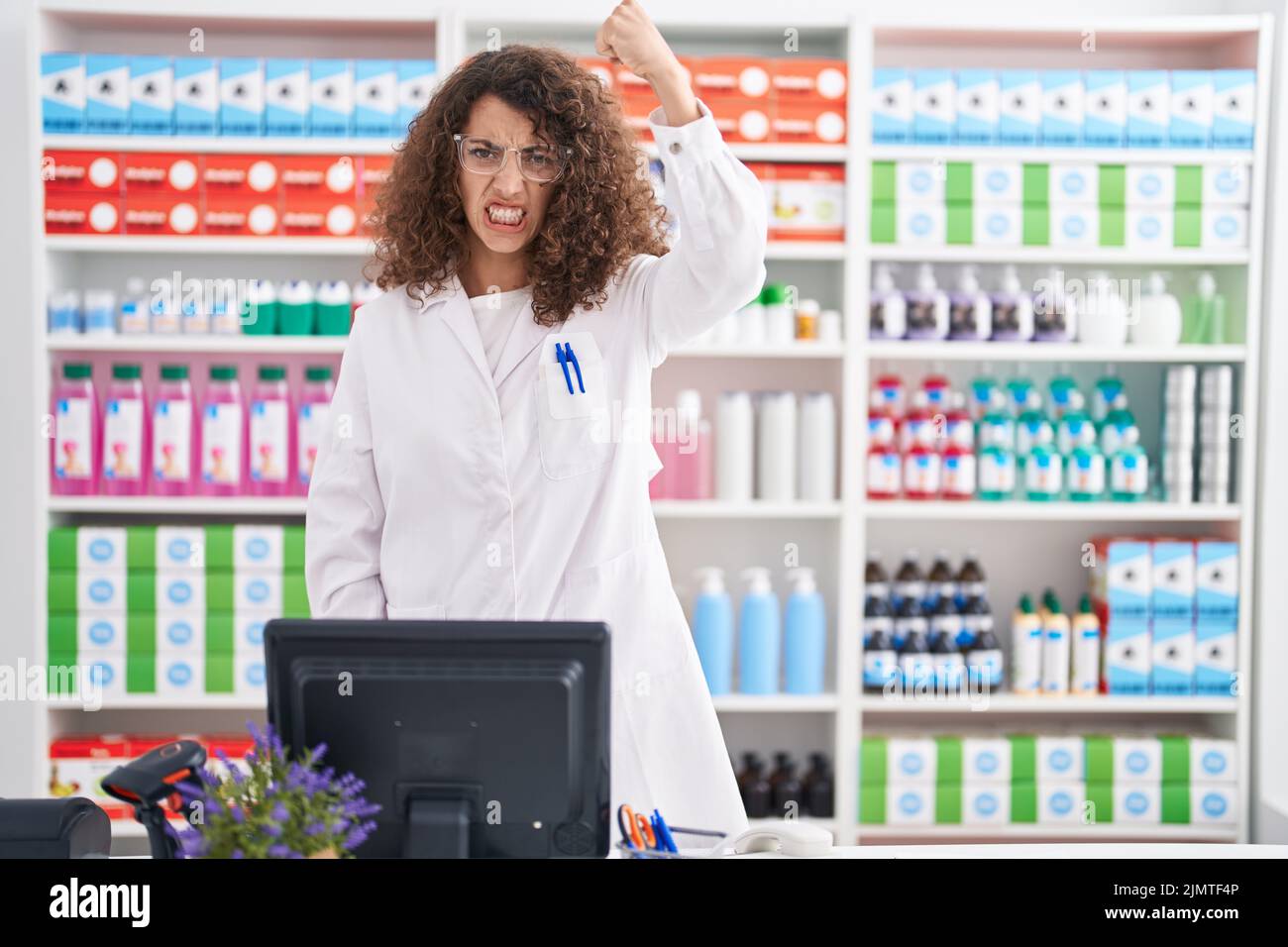 Hispanic woman with curly hair working at pharmacy drugstore angry and ...