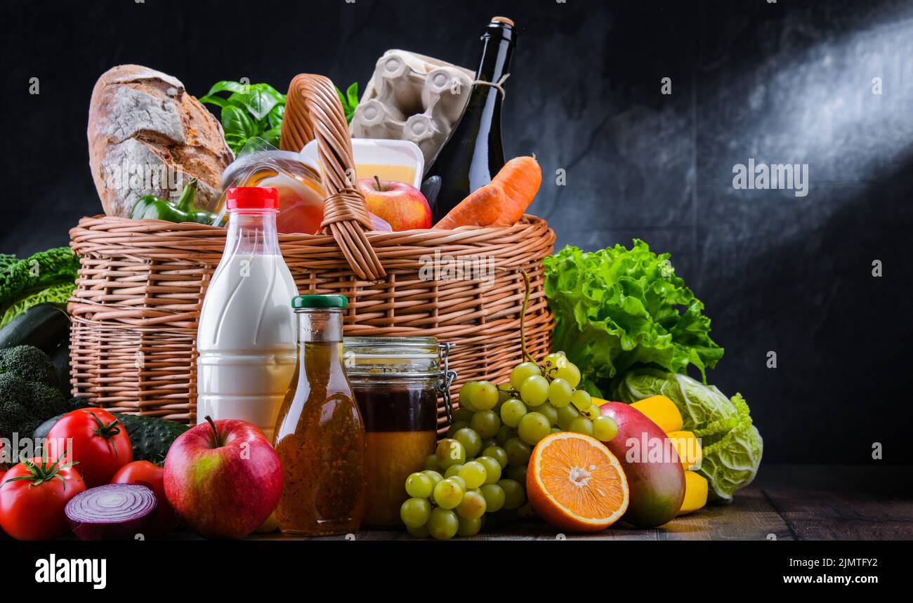 Wicker basket with assorted grocery products including fresh vegetables ...