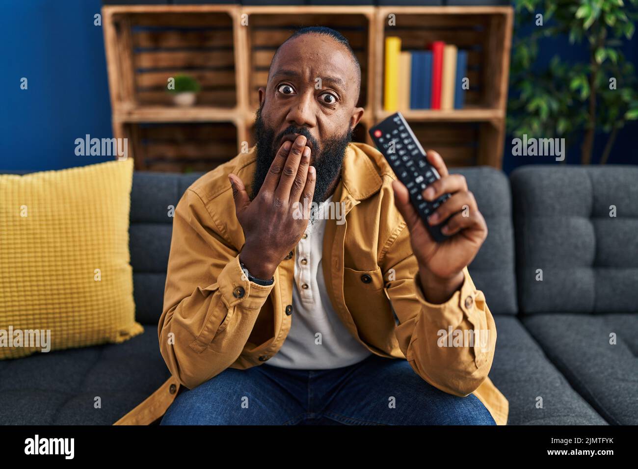 African american man holding television remote control covering mouth ...