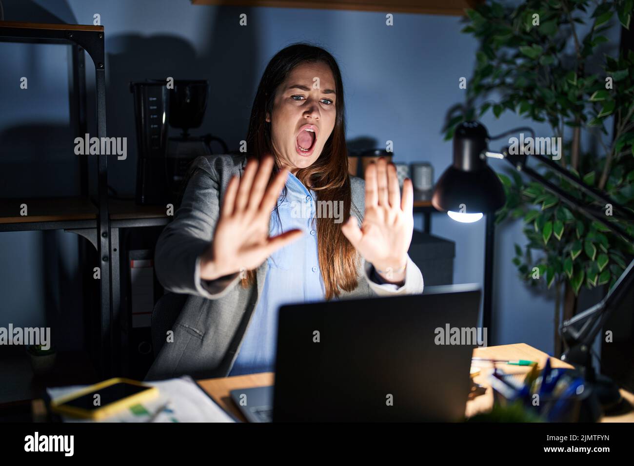 Young brunette woman working at the office at night afraid and ...