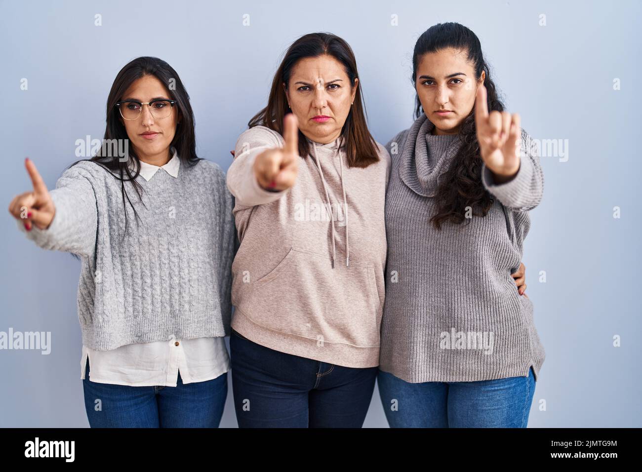 Mother and two daughters standing over blue background pointing with ...