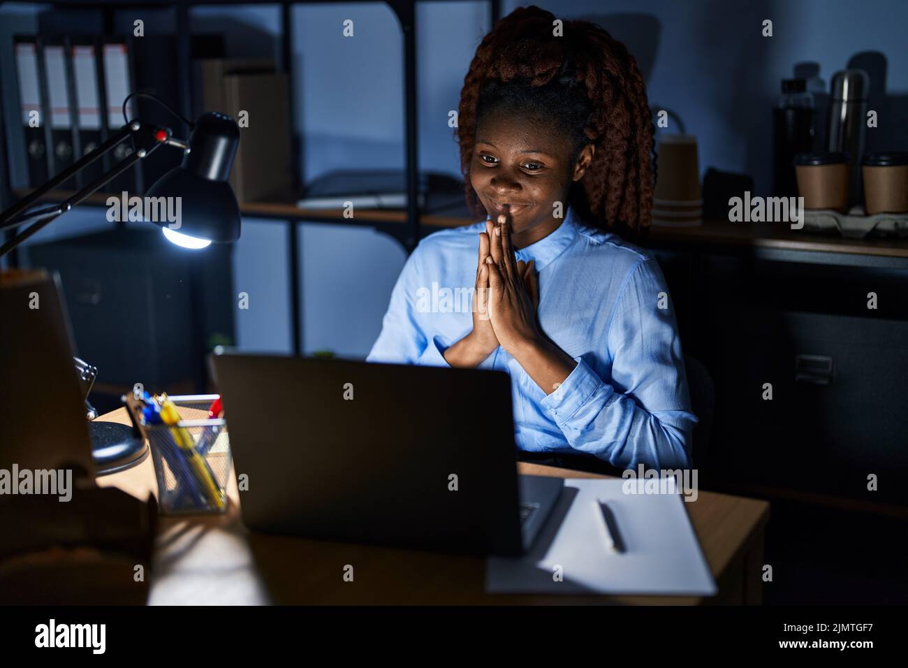 African woman working at the office at night praying with hands ...