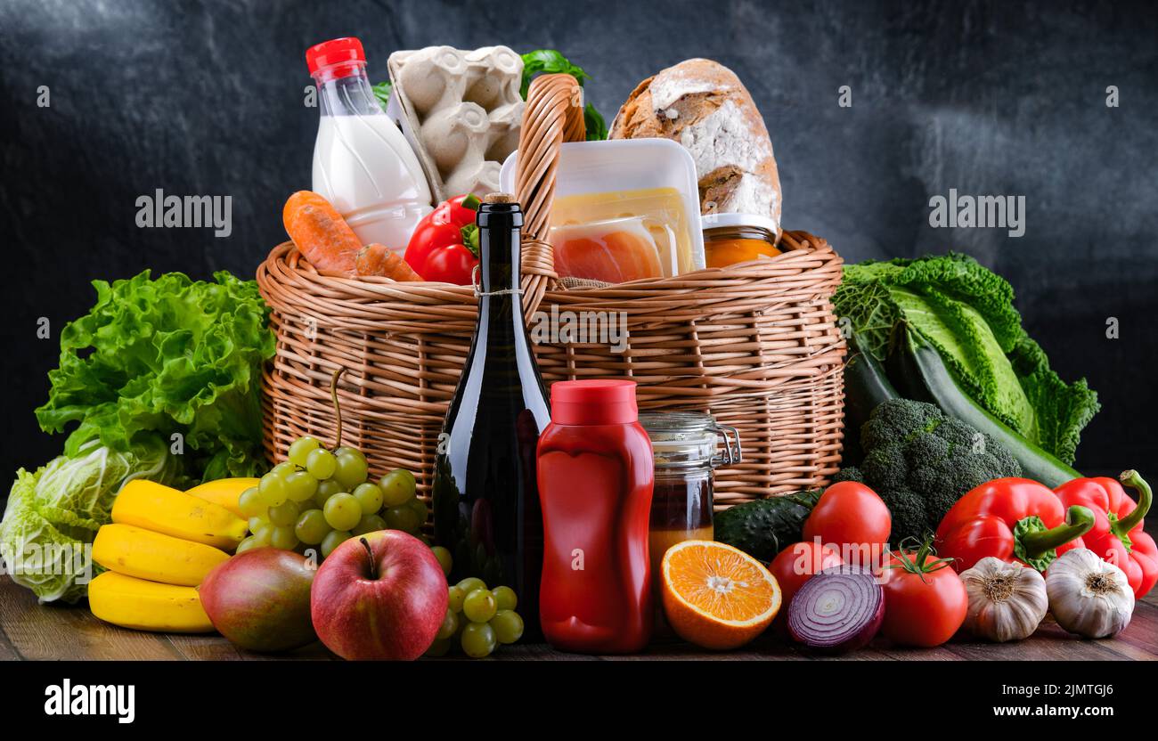 Wicker basket with assorted grocery products including fresh vegetables ...