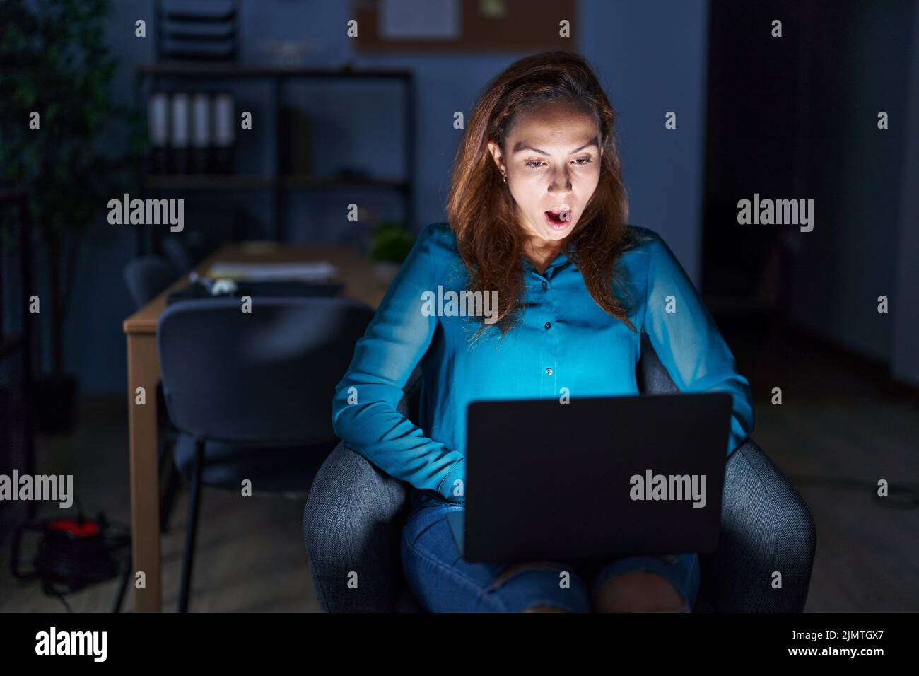 Brunette woman working at the office at night afraid and shocked with ...