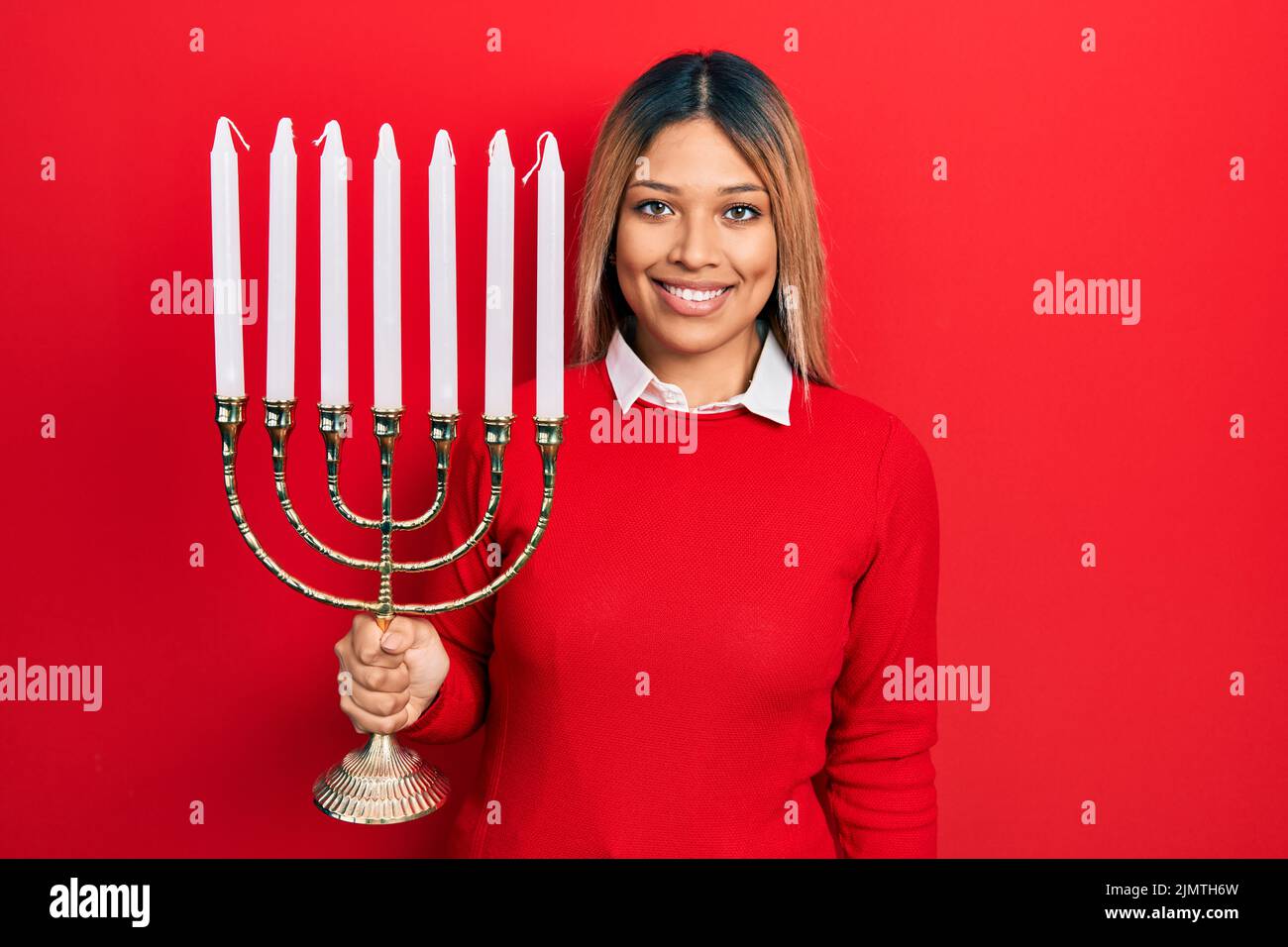 Beautiful hispanic woman holding menorah hanukkah jewish candle looking ...