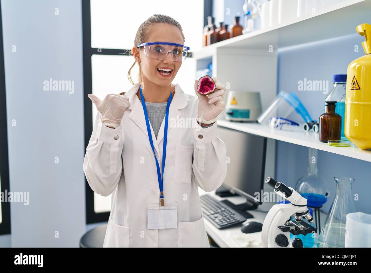 Young woman working at scientist laboratory holding geode pointing ...