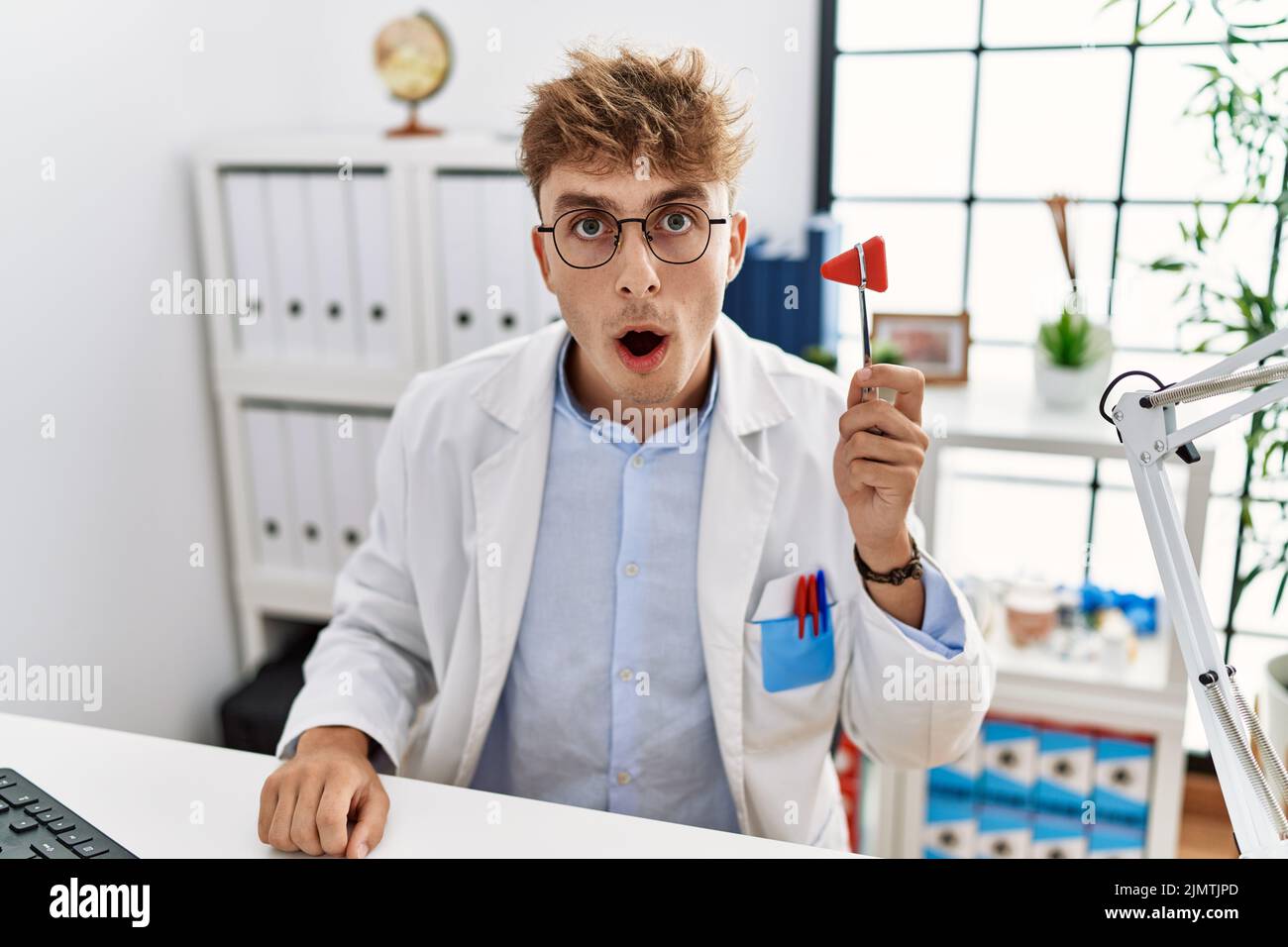 Young caucasian doctor man holding reflex hammer at the clinic scared ...