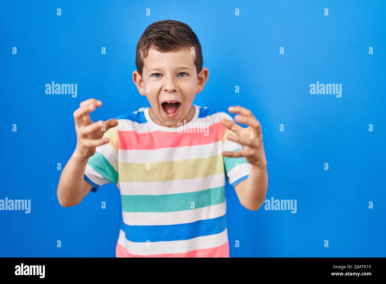 Young caucasian kid standing over blue background shouting frustrated ...
