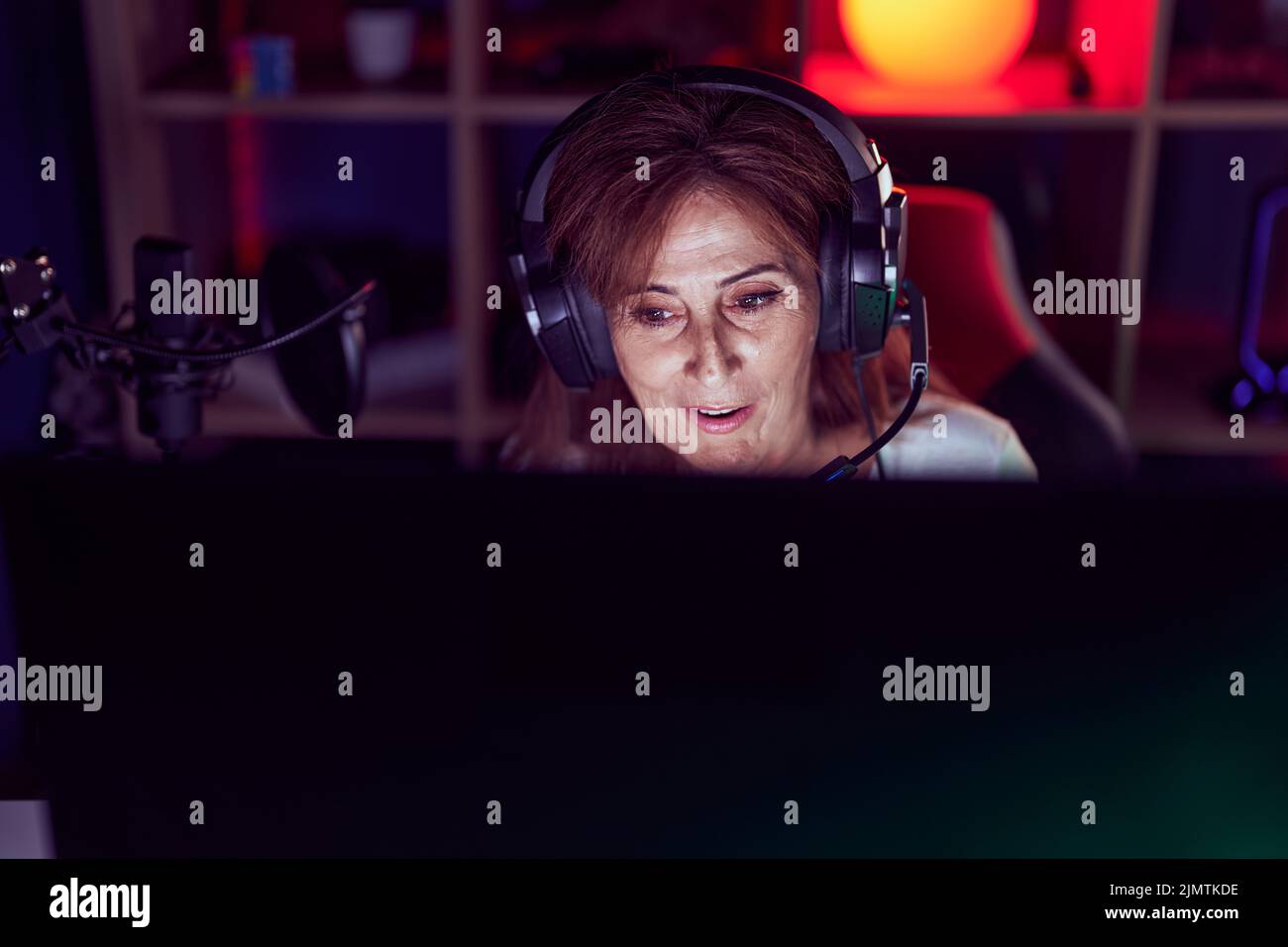 Middle age woman streamer playing video game using computer at gaming ...