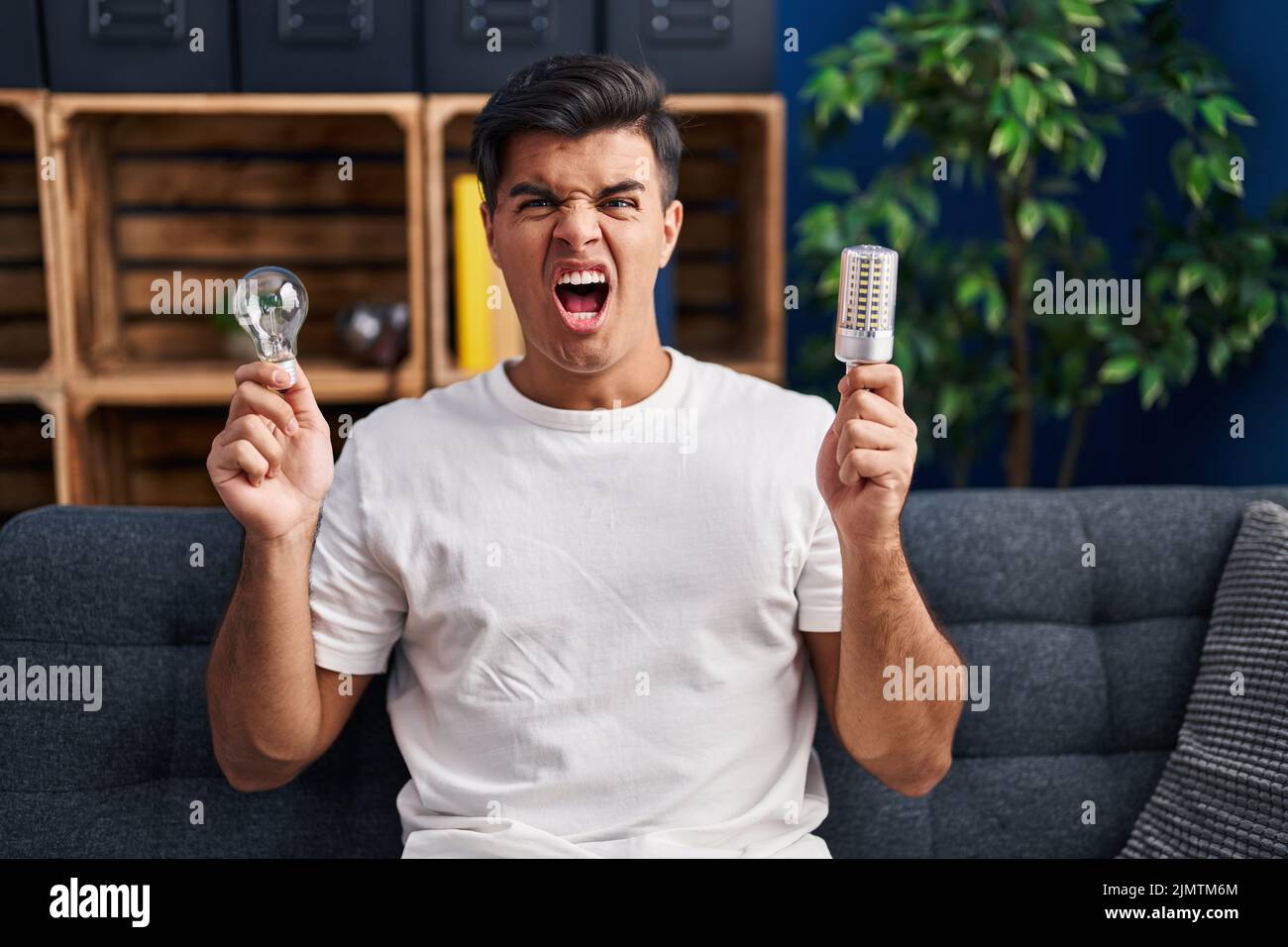 Hispanic man holding led lightbulb and incandescent bulb angry and mad ...