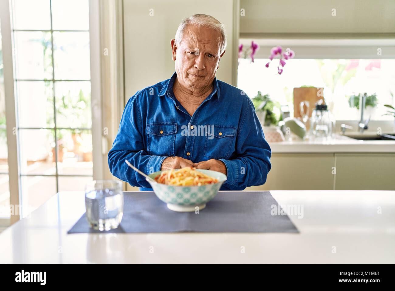 Senior man with grey hair eating pasta spaghetti at home depressed and ...