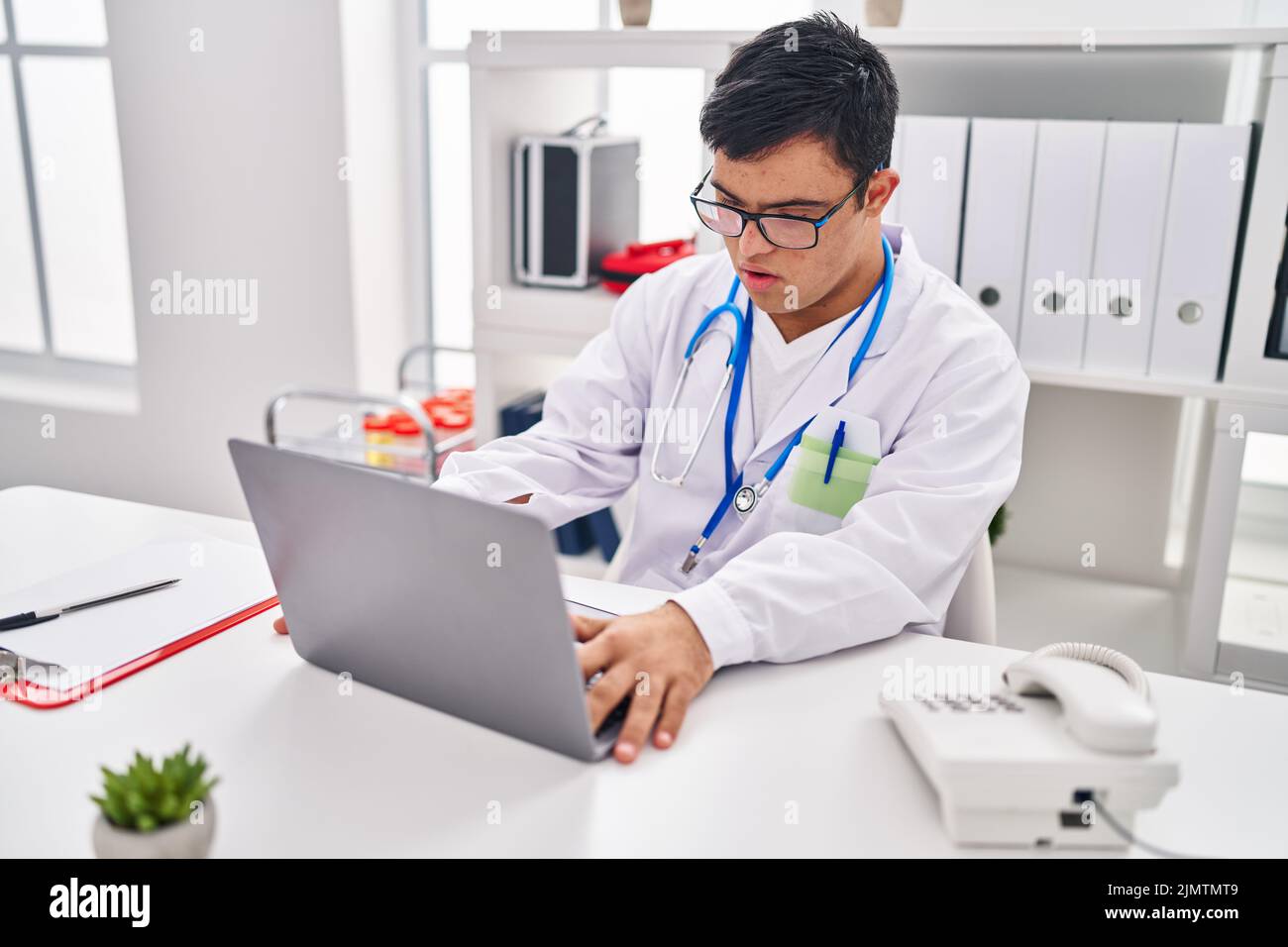Down syndrome man wearing doctor uniform using laptop working at clinic ...