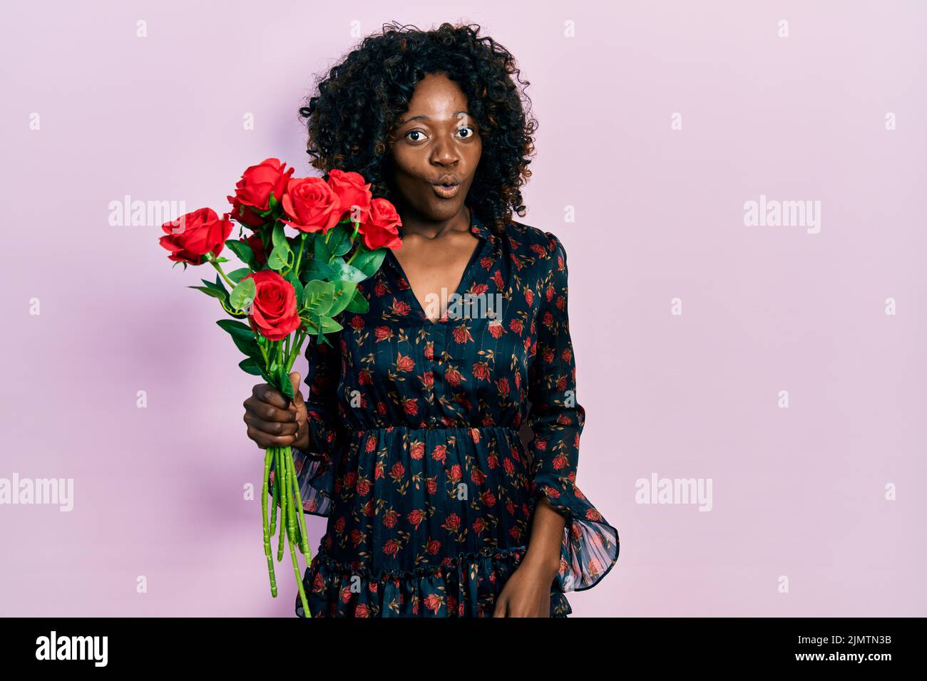 Young african american woman holding bouquet of red roses scared and ...