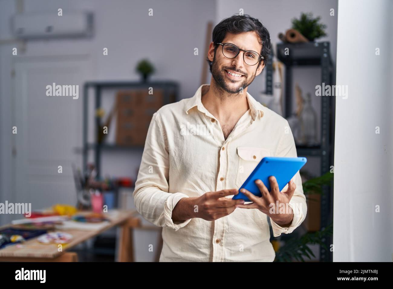 Young hispanic man artist smiling confident using touchpad at art ...