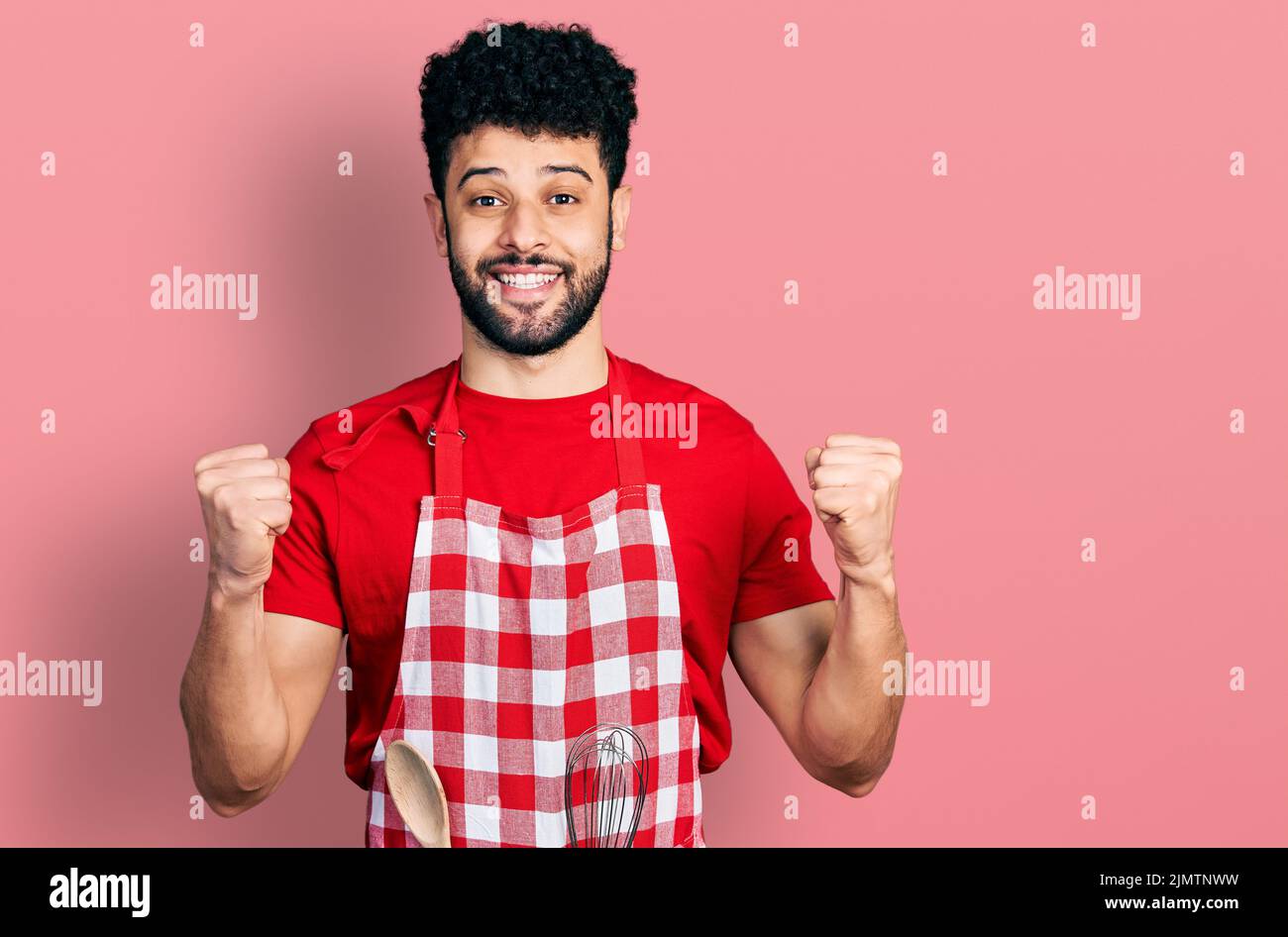 Young arab man with beard wearing cook apron celebrating surprised and ...