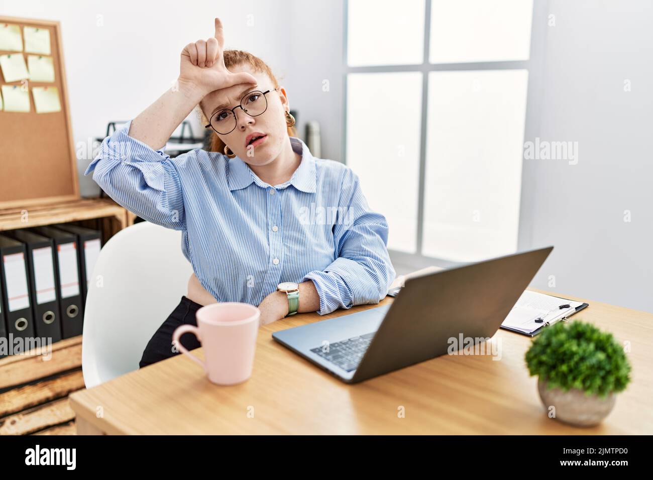 Young redhead woman working at the office using computer laptop making ...