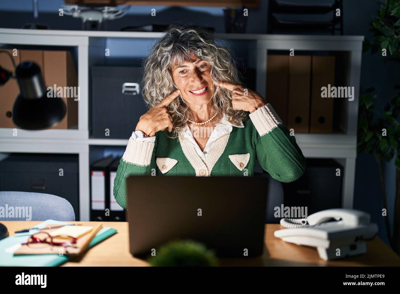 Middle age woman working at night using computer laptop smiling ...