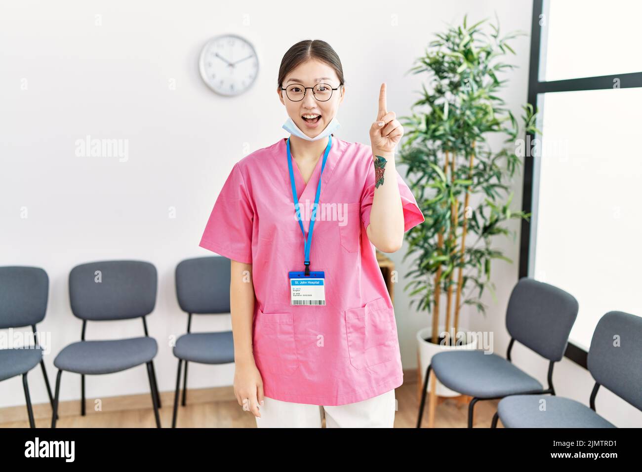 Young asian nurse woman at medical waiting room pointing finger up with ...