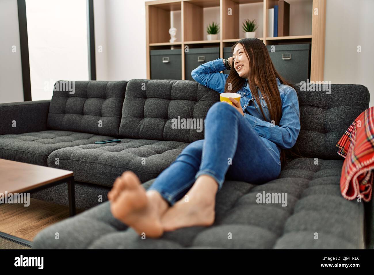 Young chinese girl drinking coffee lying on the sofa at home Stock ...