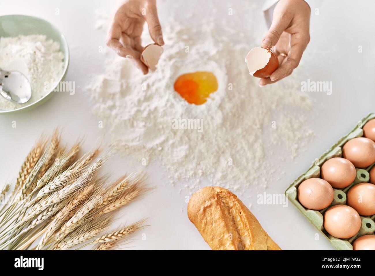 Young woman wearing cook uniform cracking egg on flour at kitchen Stock ...