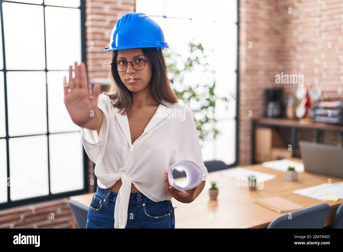 Hispanic young woman wearing architect hardhat at office with open hand ...