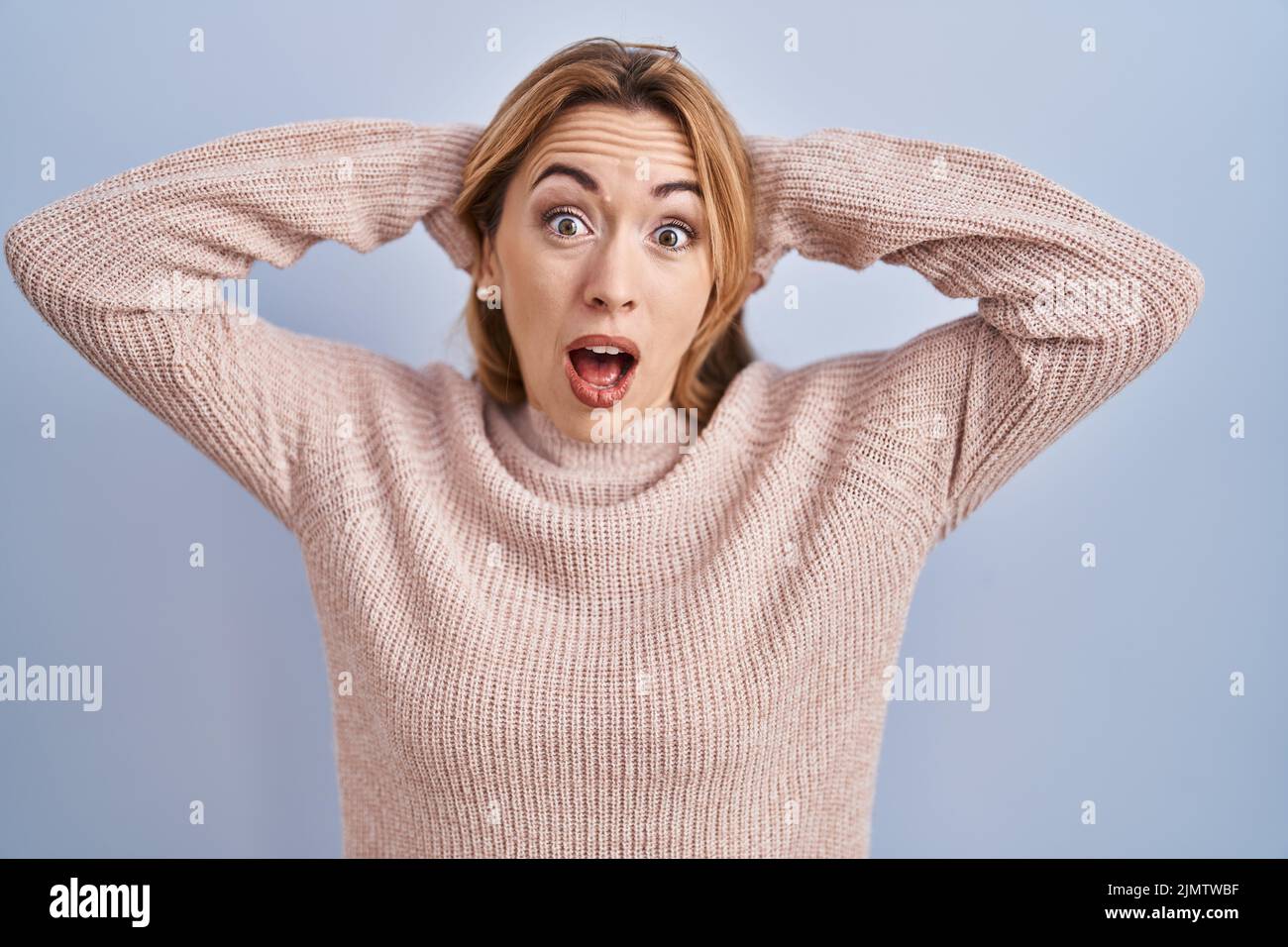 Hispanic woman standing over blue background crazy and scared with ...