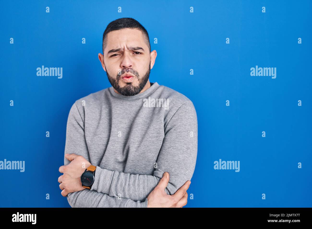 Hispanic man standing over blue background shaking and freezing for ...