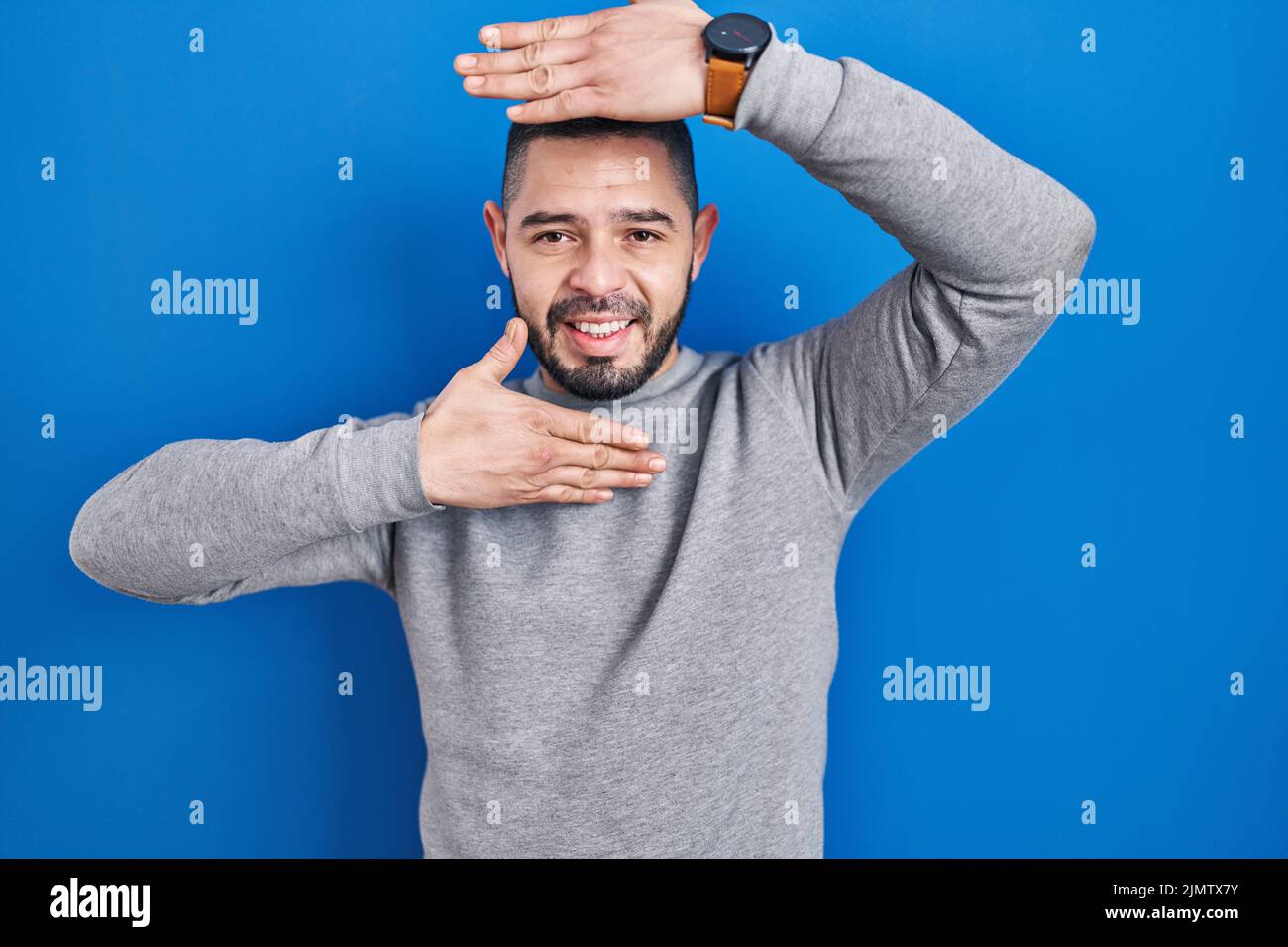 Hispanic man standing over blue background smiling cheerful playing ...