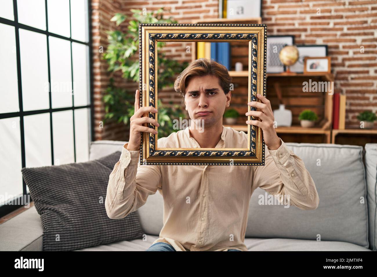 Young man holding empty frame skeptic and nervous, frowning upset ...