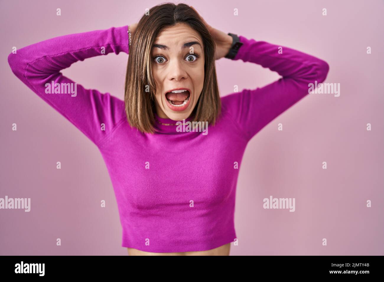 Hispanic woman standing over pink background crazy and scared with ...