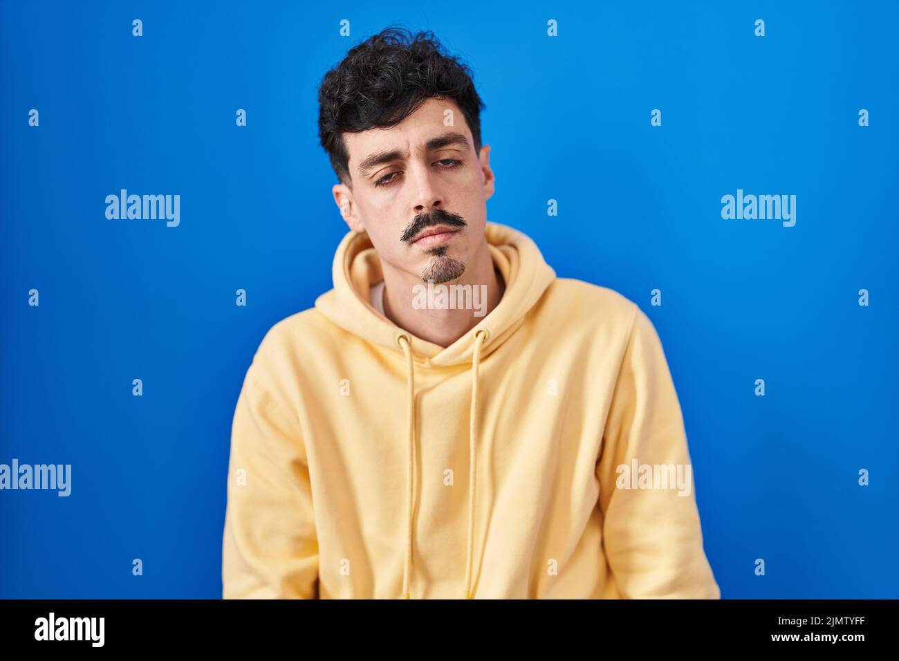 Hispanic man standing over blue background looking sleepy and tired ...