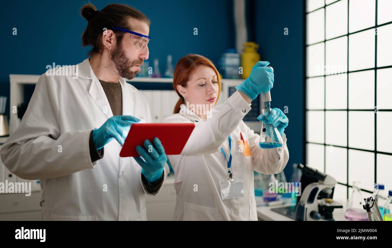 Man and woman wearing sciencist uniform using touchpad at laboratory ...