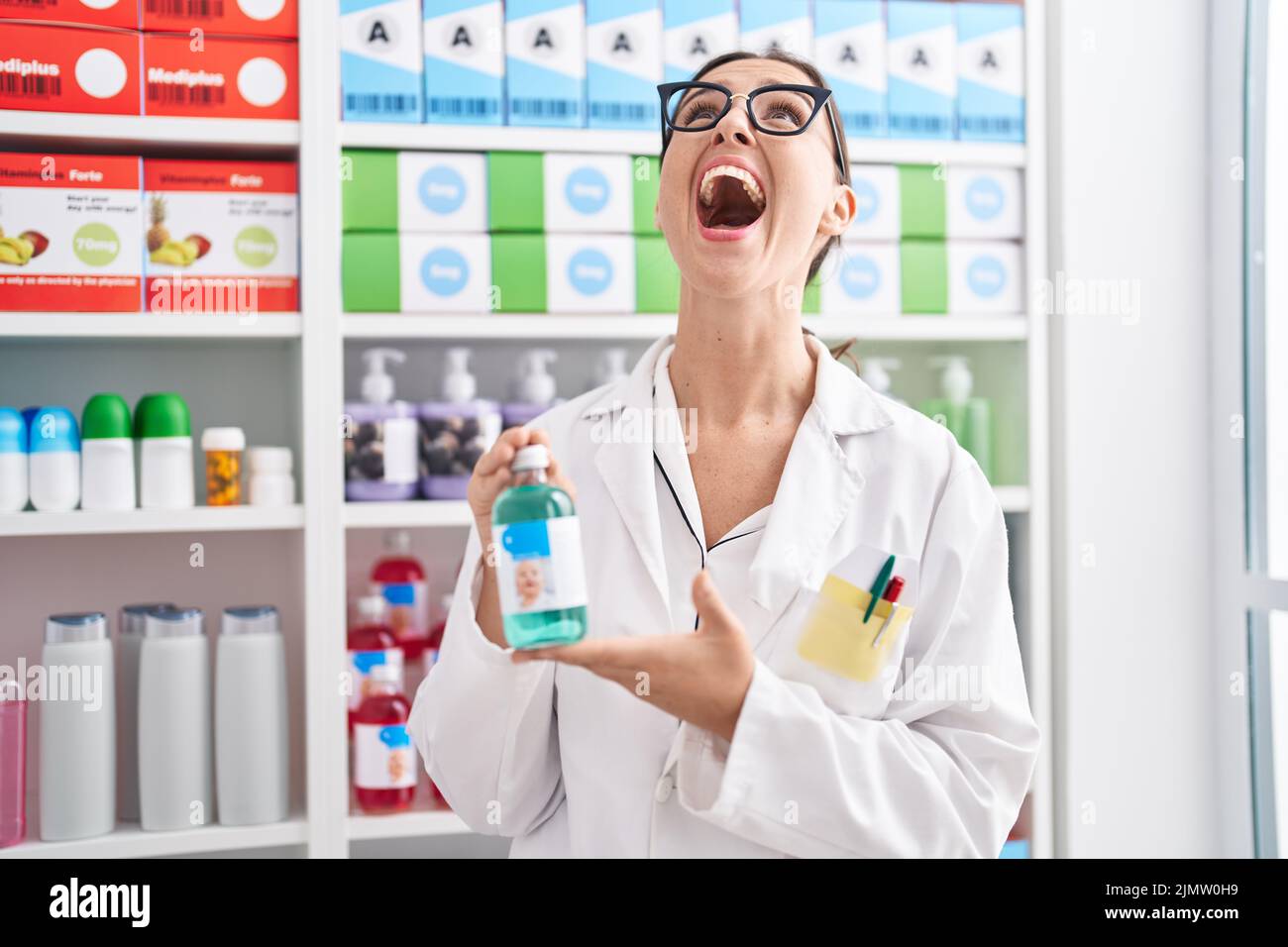 Brunette woman working at pharmacy drugstore holding cough syrup angry ...