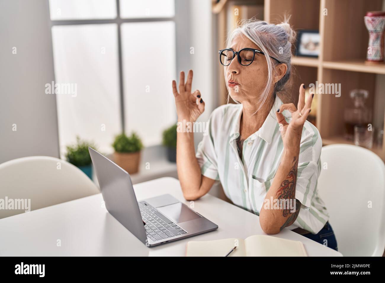 Middle age grey-haired woman doing yoga exercise sitting on table at ...
